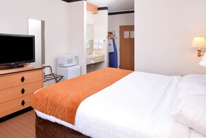 Quarto de hotel com cama, televisão, micro-ondas, cômoda e banheiro visível por uma porta aberta.