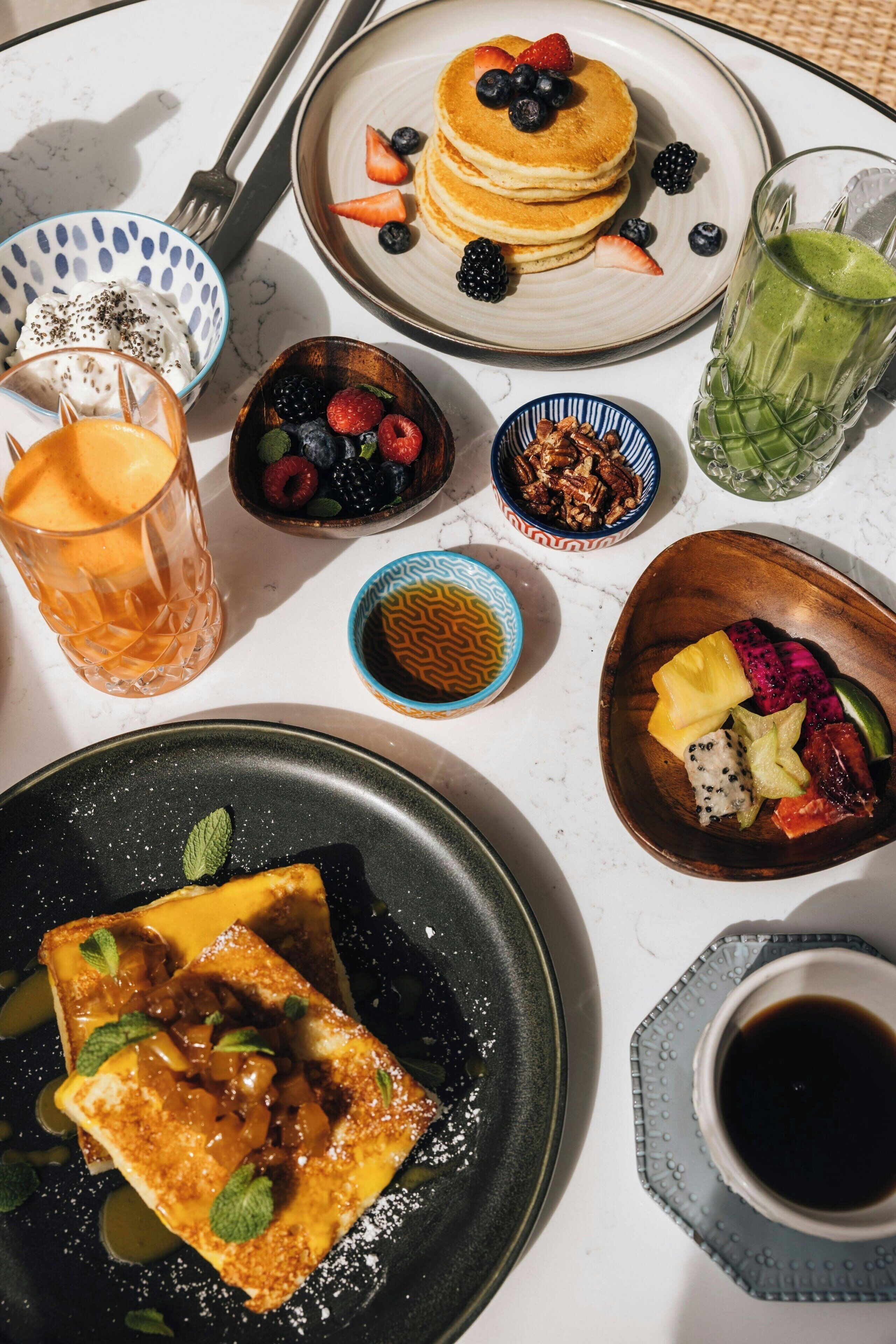 Mesa posta para o café da manhã com panquecas, frutas e bebidas.
