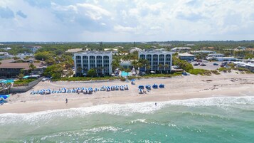 Um hotel à beira-mar com vários edifícios, uma praia de areia e área de piscina.