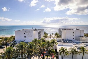 Um hotel à beira-mar com dois edifícios brancos imponentes, uma praia e palmeiras.