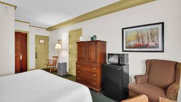 Quarto de hotel com uma cama, cômoda de madeira, televisão, cadeira e um quadro na parede.
