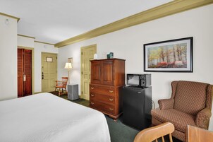 Quarto de hotel com uma cama, cômoda de madeira, televisão, cadeira e um quadro na parede.