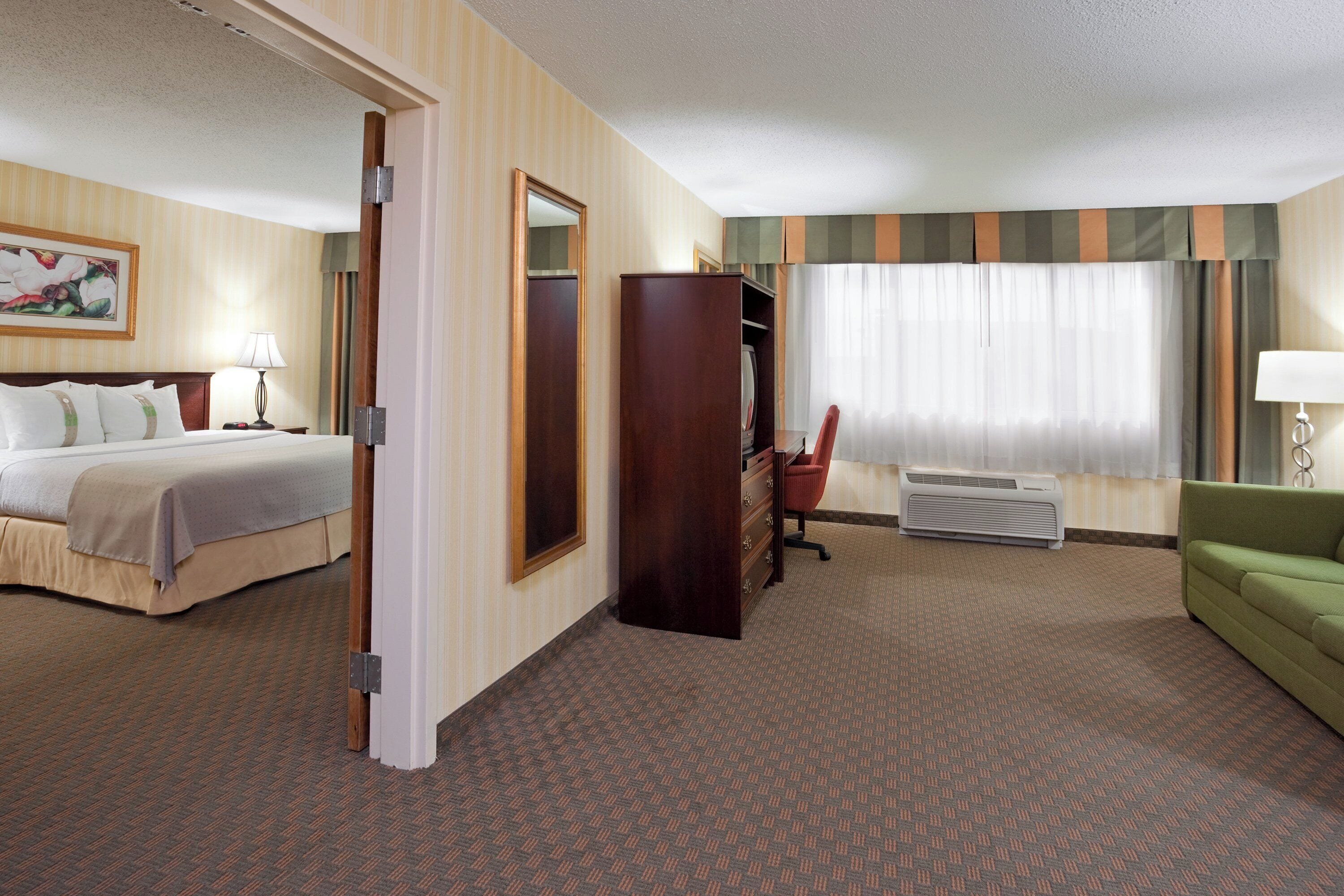 Quarto de hotel com cama, escrivaninha, cadeira, guarda-roupa e sofá verde.