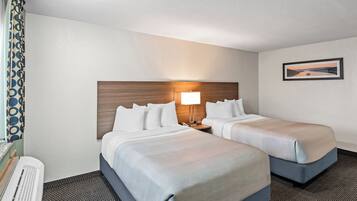 Quarto de hotel com duas camas, uma mesa de cabeceira com abajur, um quadro na parede e um tapete estampado.