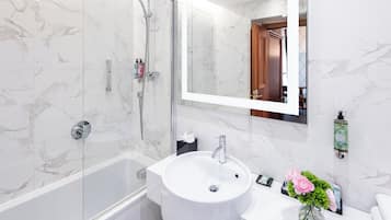 Uma casa de banho moderna com chuveiro envidraçado, lavatório branco e espelho grande.
