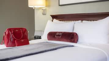Quarto de hotel com cama bem arrumada, uma bolsa vermelha, um travesseiro vermelho e uma luminária fixada na parede.