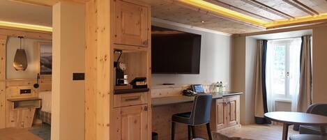 Quarto de hotel moderno com lambris de madeira, televisão de tela plana, área de refeições com mesa e cadeiras, e um espaço de estar aconchegante.