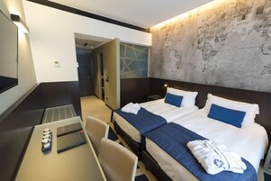 Quarto de hotel com duas camas, uma escrivaninha com um laptop e um espaço para sentar.