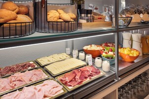 Buffet com diversos itens de comida, incluindo pães, doces, carnes, queijos e frutas.