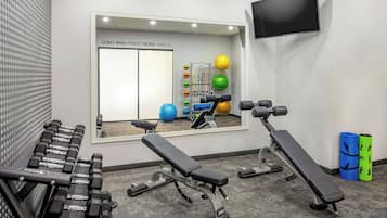 Academia com bancos, halteres, bolas de exercício e um espelho.
