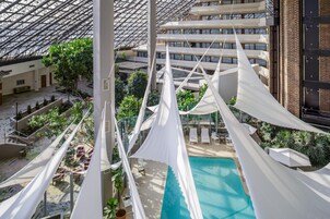 Um hotel alto com piscina no terraço, jardim interno e vista para a paisagem urbana.