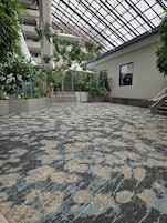 Um átrio interno com piso estampado, grandes janelas e plantas.