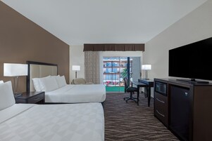 Quarto de hotel com duas camas, uma escrivaninha, televisão e vista para uma varanda com área de estar ao ar livre.
