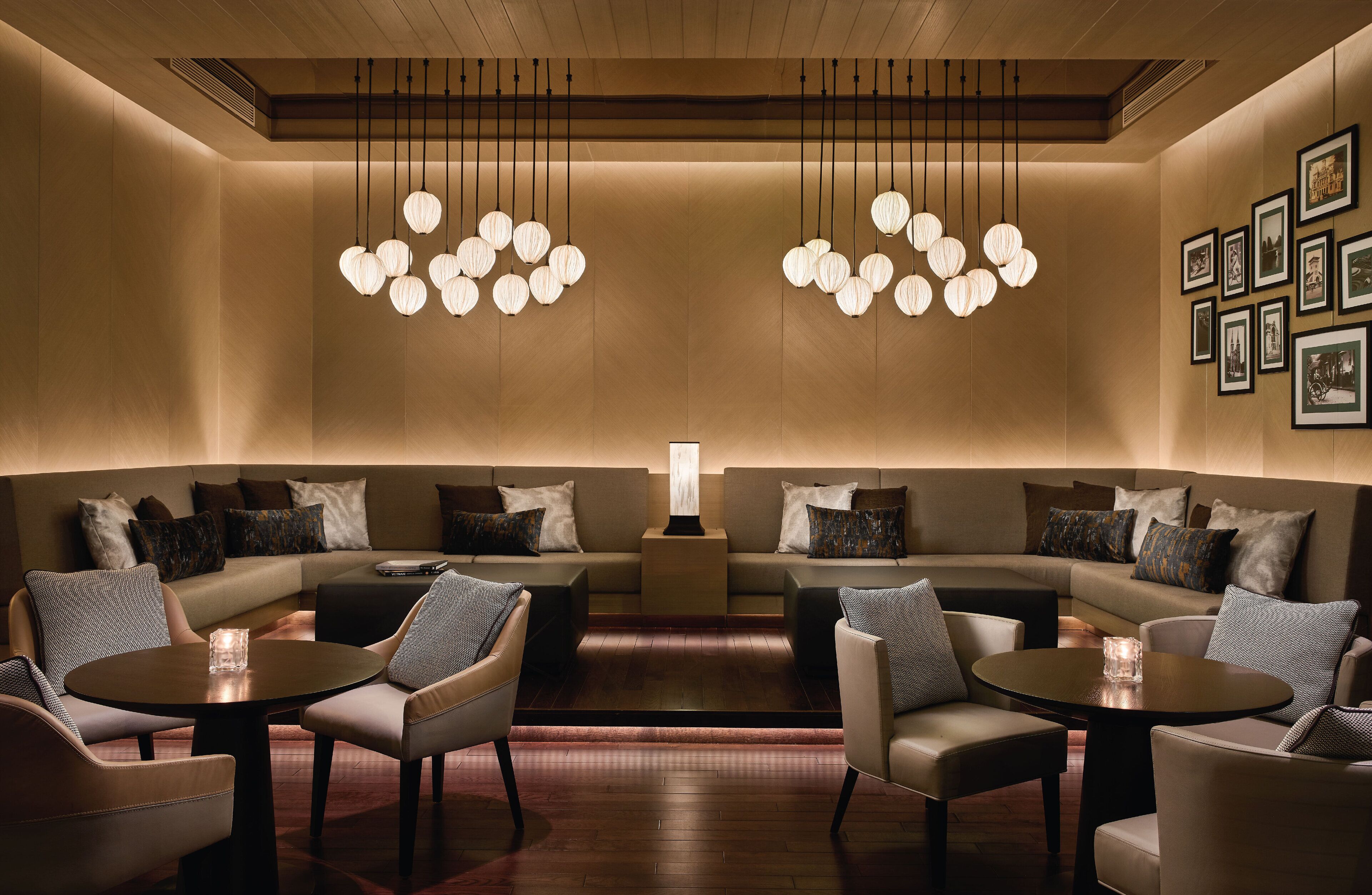 Uma área de estar moderna com sofás, poltronas e uma mesa de centro, com iluminação pendente e quadros nas paredes.