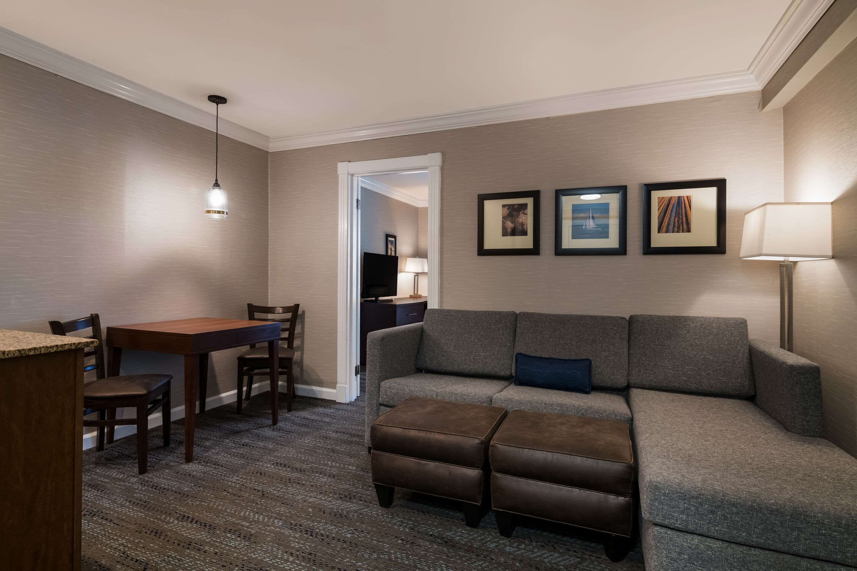 Quarto de hotel com área de refeições, sofá e televisão ao fundo.