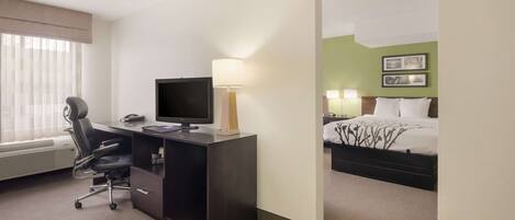 Quarto de hotel com escrivaninha, cadeira, televisão, abajur e cama com dossel.
