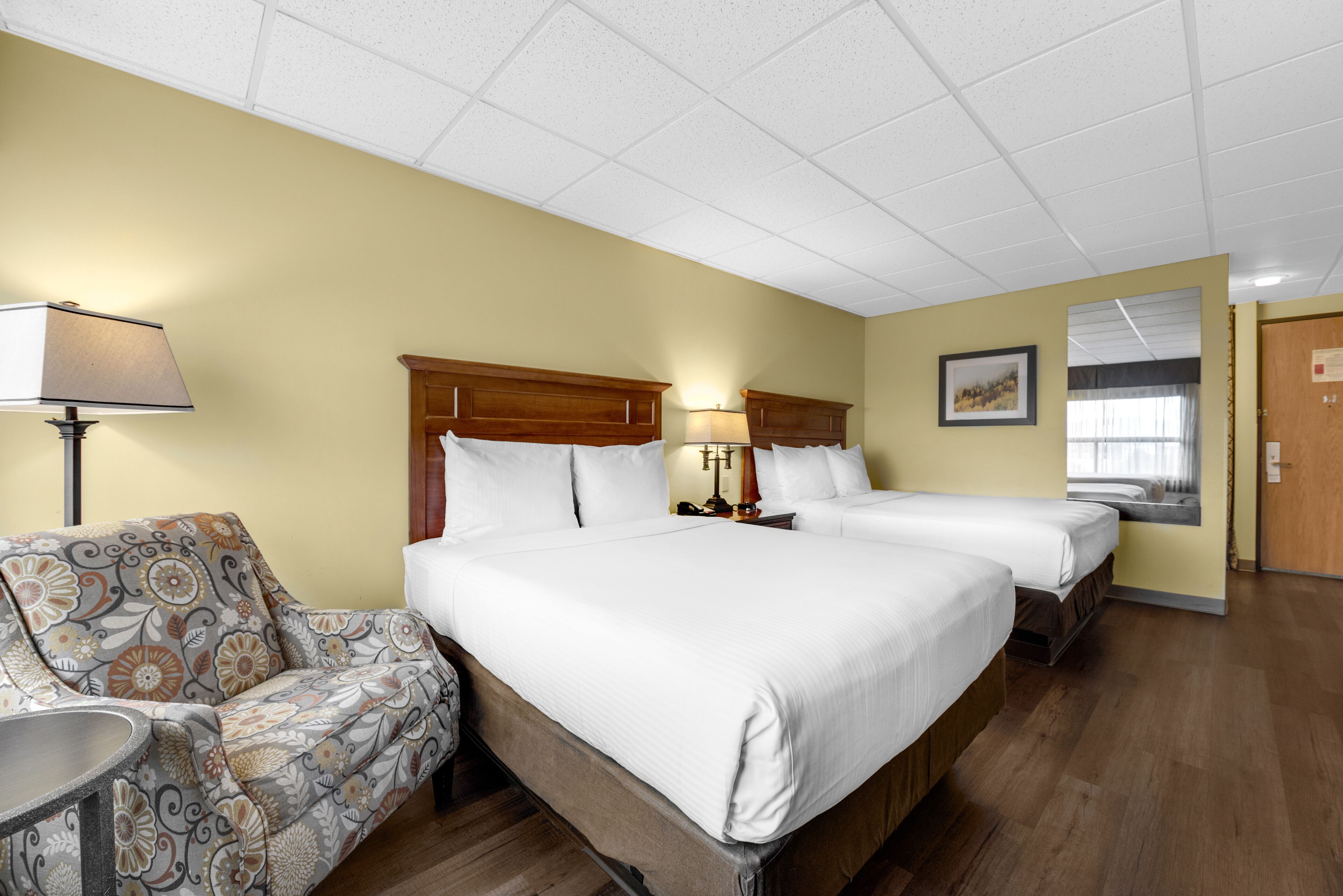 Quarto de hotel com duas camas, um sofá, uma luminária e um quadro na parede.