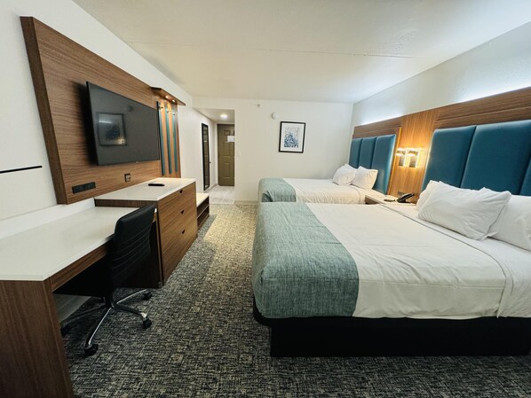 Quarto de hotel com escrivaninha, duas camas, televisão e um quadro na parede.