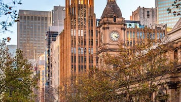Uma rua urbana com um edifício histórico, apresentando uma torre do relógio, e um moderno arranha-céu ao fundo.