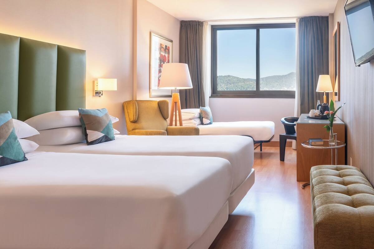 Quarto de hotel com duas camas, um sofá, uma mesinha e uma televisão.