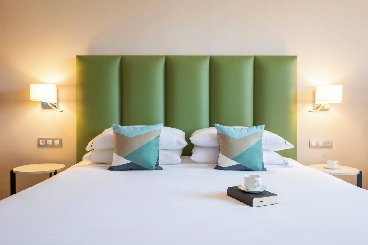 Quarto de hotel com uma cama grande, duas mesas de cabeceira e cabeceira estofada verde.