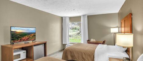 Quarto de hotel com duas camas, televisão, escrivaninha com micro-ondas e janela com cortinas.