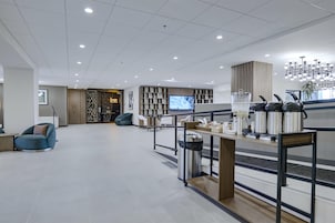 Um hall moderno com assentos, um espaço para café e uma televisão.