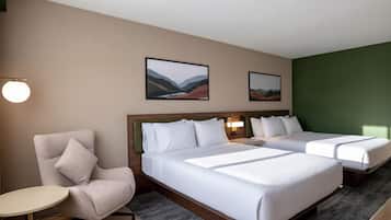 Quarto de hotel com duas camas, uma cadeira, uma mesinha e duas luminárias fixadas na parede.