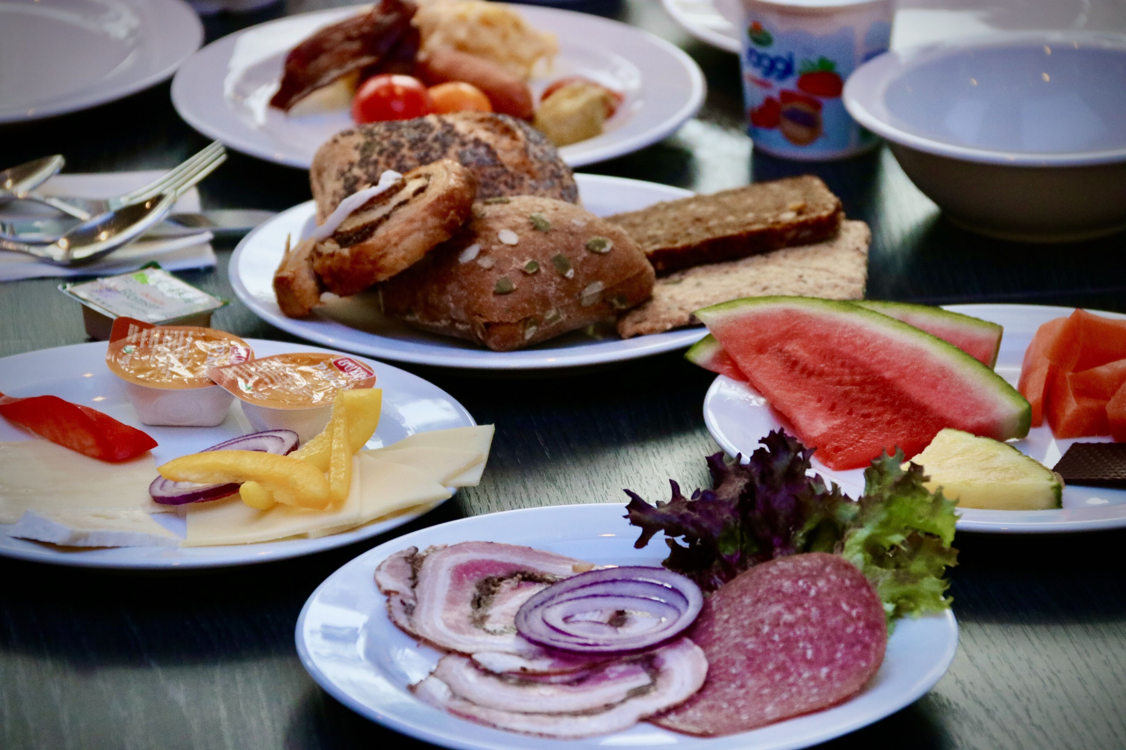 Uma mesa com diversos alimentos, incluindo pão, queijo, fatias de carne e legumes.