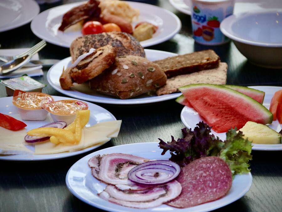 Uma mesa com diversos alimentos, incluindo pão, queijo, fatias de carne e legumes.
