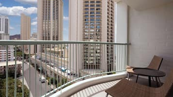 Varanda com cadeira e mesa de vime, com vista para um horizonte urbano repleto de prédios altos.