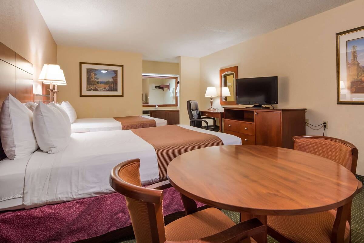 Quarto de hotel com duas camas, televisão, mesa de jantar e um quadro na parede.