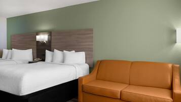 Quarto de hotel com cama, sofá, mesa de cabeceira com abajur e luminária na parede.