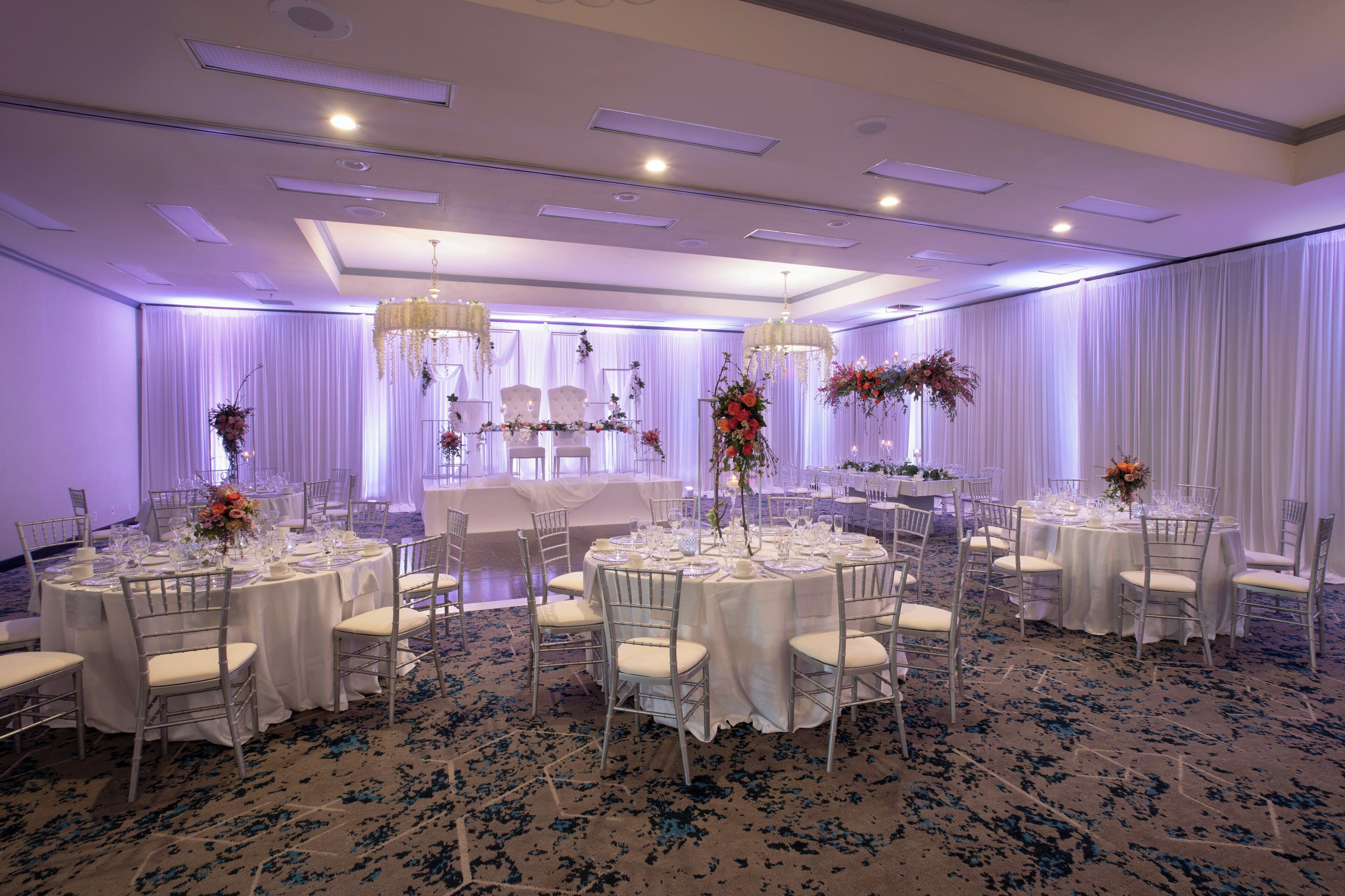 Salão de banquetes com mesas redondas, toalhas brancas e cadeiras.