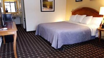 Quarto de hotel com cama, escrivaninha com computador, janela e quadro na parede.