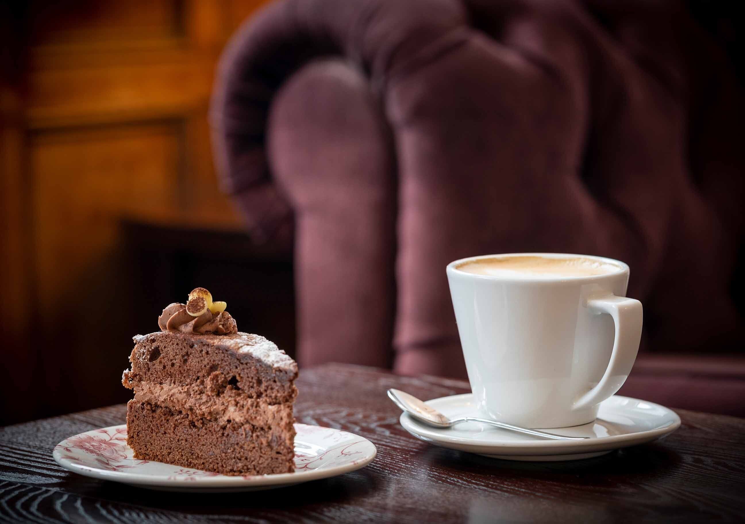 Uma fatia de bolo de chocolate com chantilly e uma xícara de café sobre um pires.