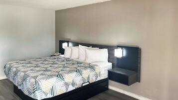 Quarto de hotel com cama, mesa de cabeceira e luminária fixada na parede.