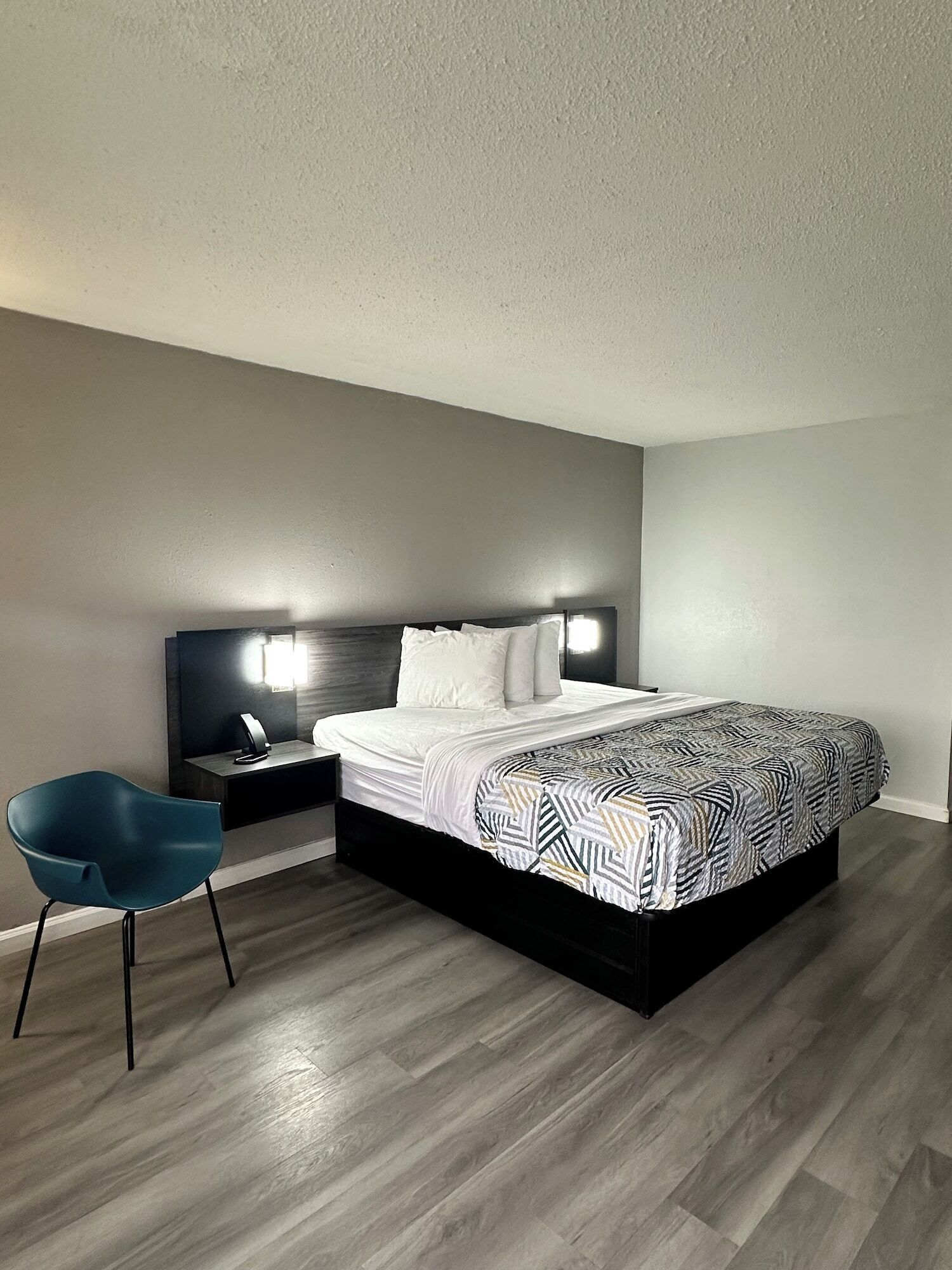 Quarto de hotel moderno com uma cama grande, uma mesinha de cabeceira, uma cadeira e um criado-mudo.