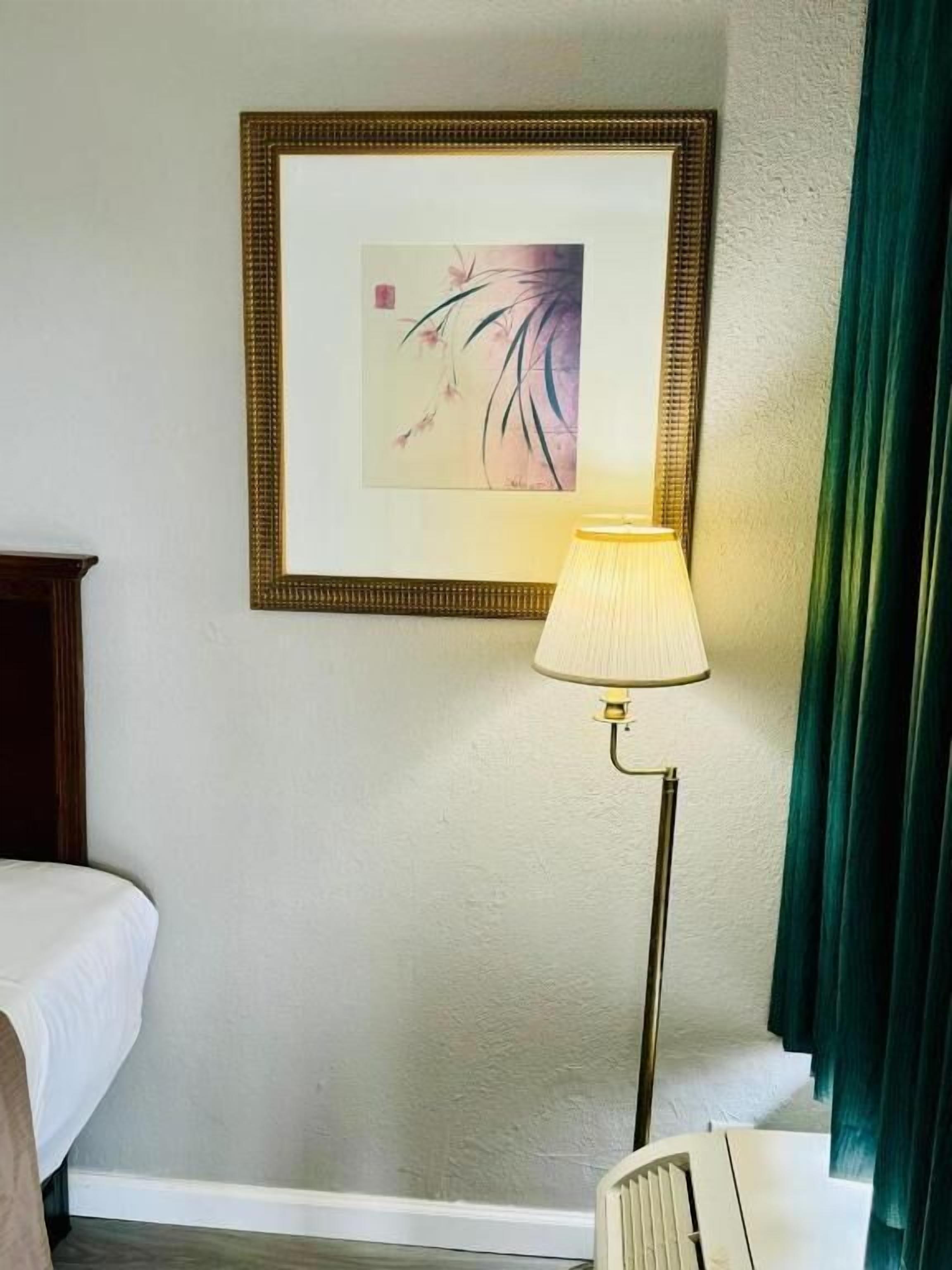 Quarto com cama, luminária na parede e uma obra de arte emoldurada.