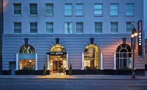 Um hotel com fachada moderna, janelas em arco e uma placa com a inscrição 'HOTEL zeta'.