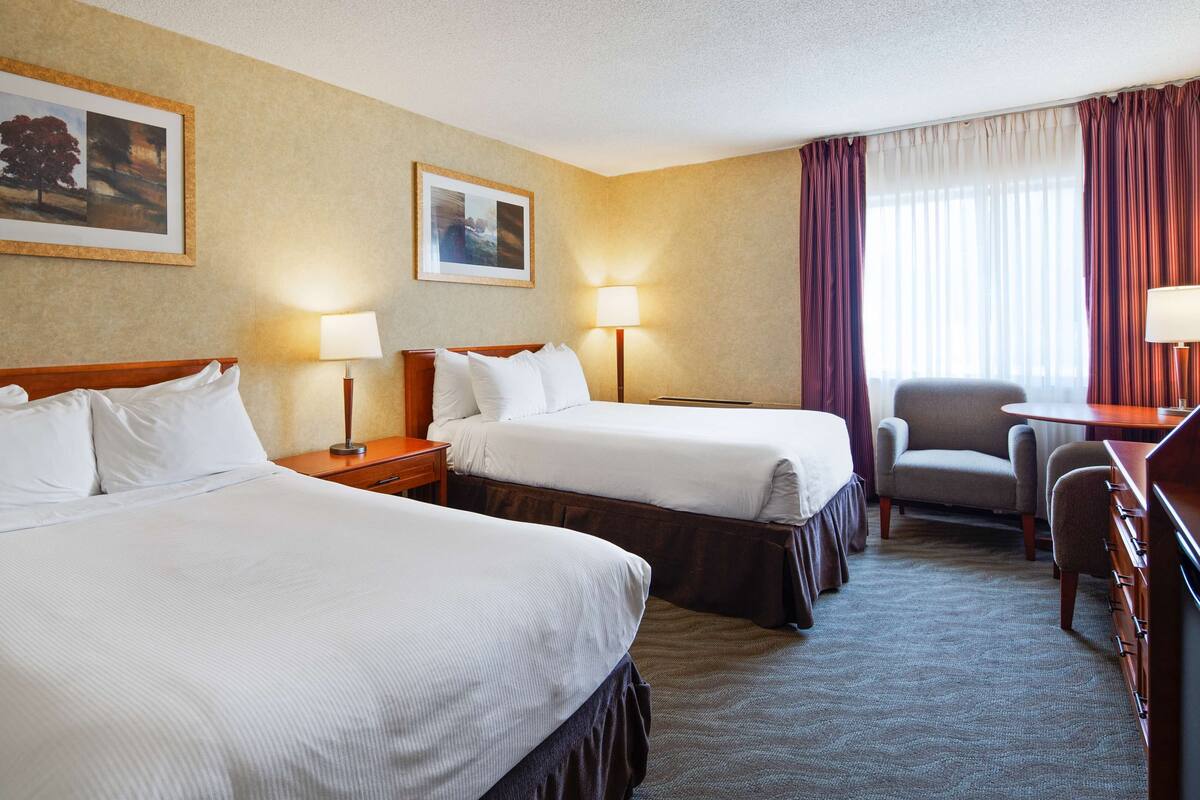 Quarto de hotel com duas camas, uma escrivaninha, uma cadeira e duas luminárias.