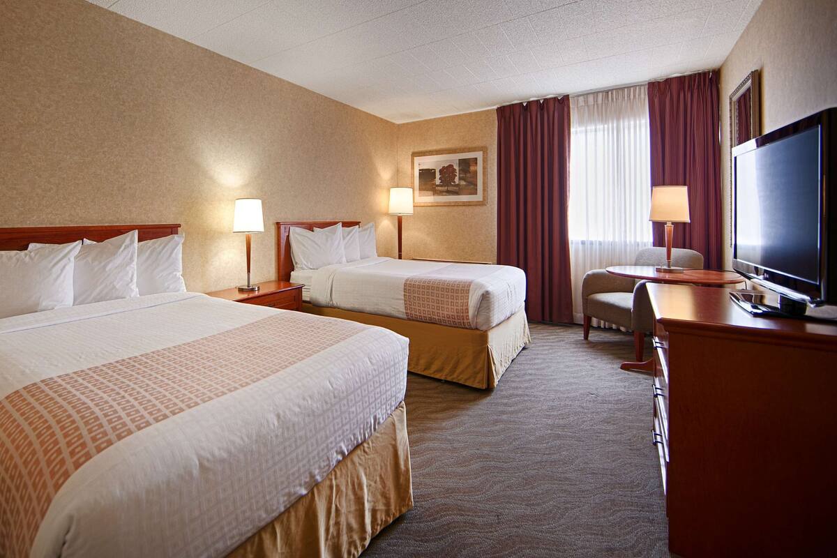 Quarto de hotel com duas camas, televisão, secretária e uma cadeira.