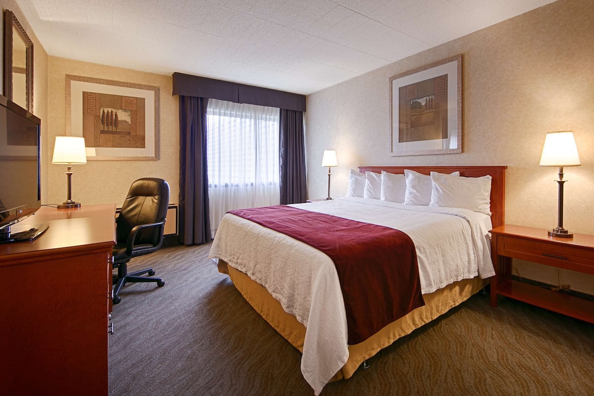 Quarto de hotel com uma cama grande, uma escrivaninha, uma cadeira, uma televisão e duas luminárias.