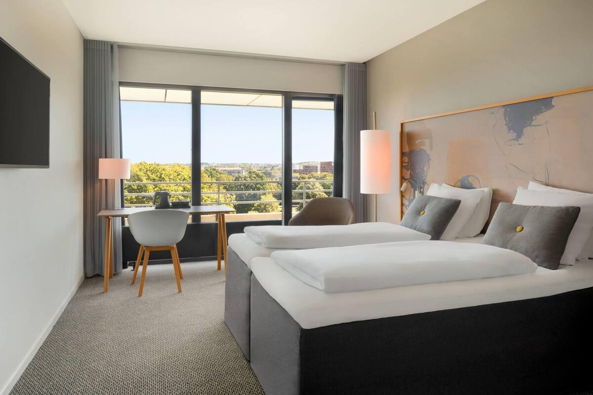 Quarto de hotel com uma cama grande, uma escrivaninha, uma cadeira e vista para a cidade.