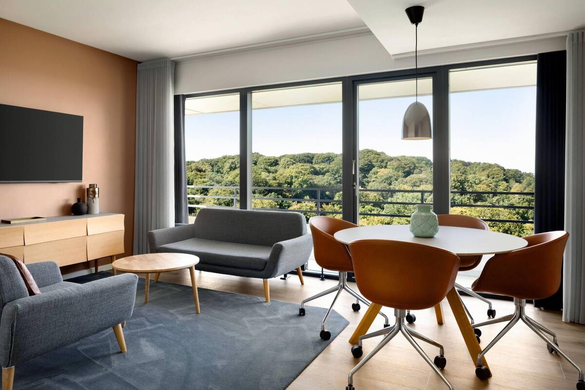 Uma sala de estar moderna com uma janela grande, um sofá, uma mesa de centro e uma área de jantar com cadeiras.