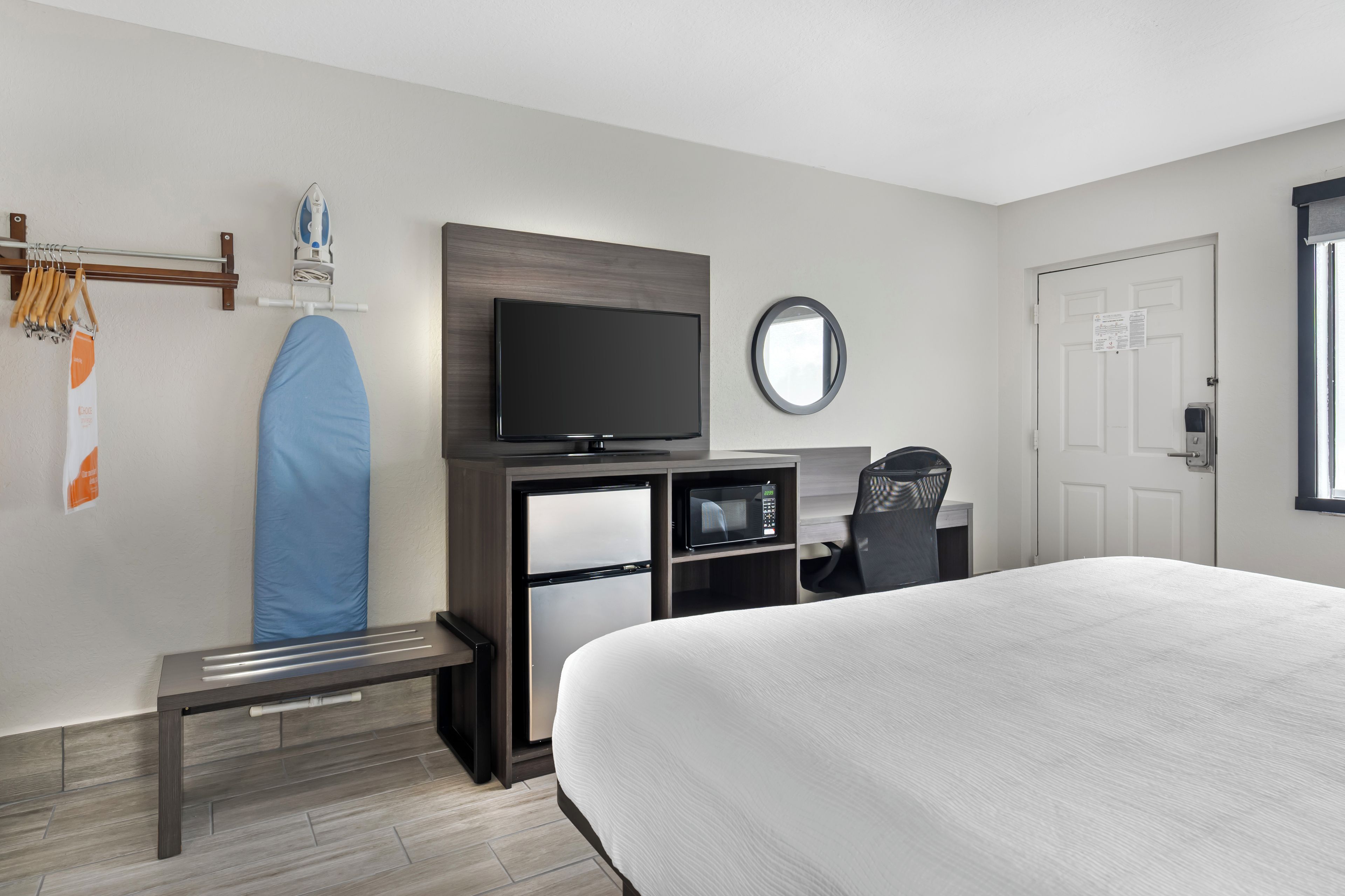 Quarto de hotel com cama, televisão, micro-ondas, um banco e porta.