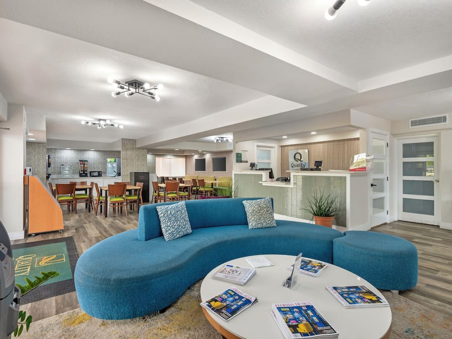Um interior moderno com um sofá azul curvo, uma mesa de centro redonda com revistas e uma área de cozinha ao fundo.