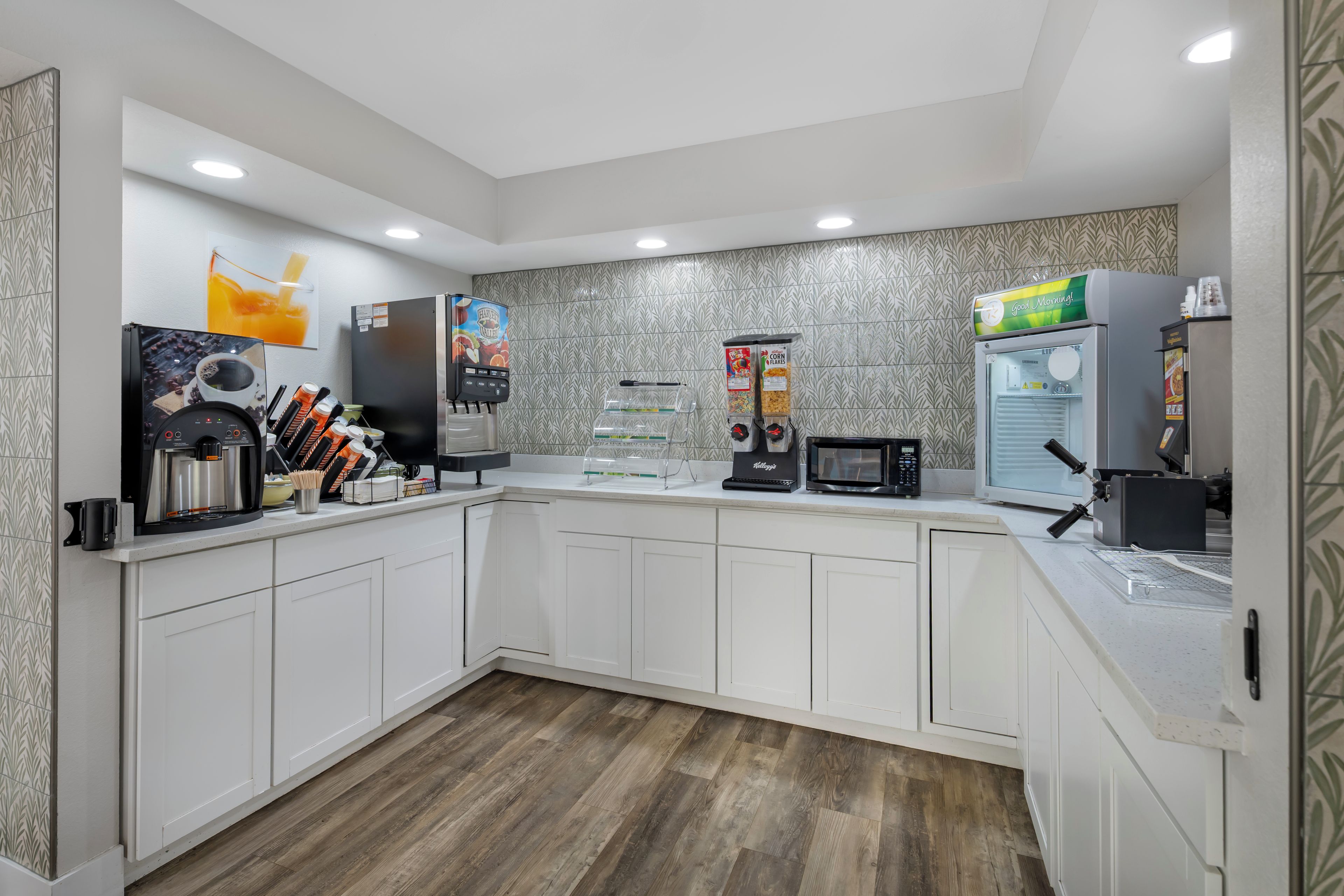 Uma cozinha moderna com armários brancos, máquina de café, micro-ondas e geladeira.