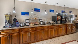 Uma cozinha de hotel com buffet, incluindo máquina de waffles, cafeteira e diversos alimentos.