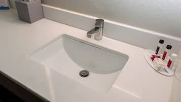Uma pia de banheiro com uma torneira moderna, uma caixa de lenços e produtos de higiene no balcão.